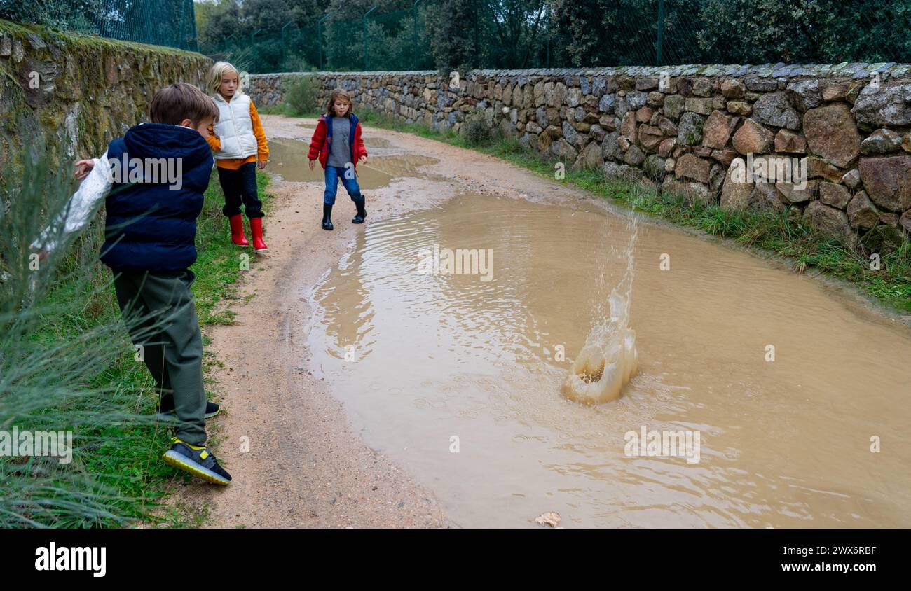 Children playing outside throwing stones into a large puddle Stock ...