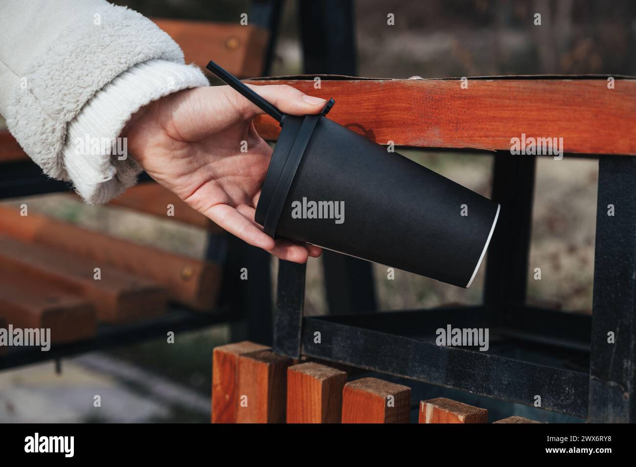 woman hand throws a recyclable cardboard cup of coffee into a trash can ...