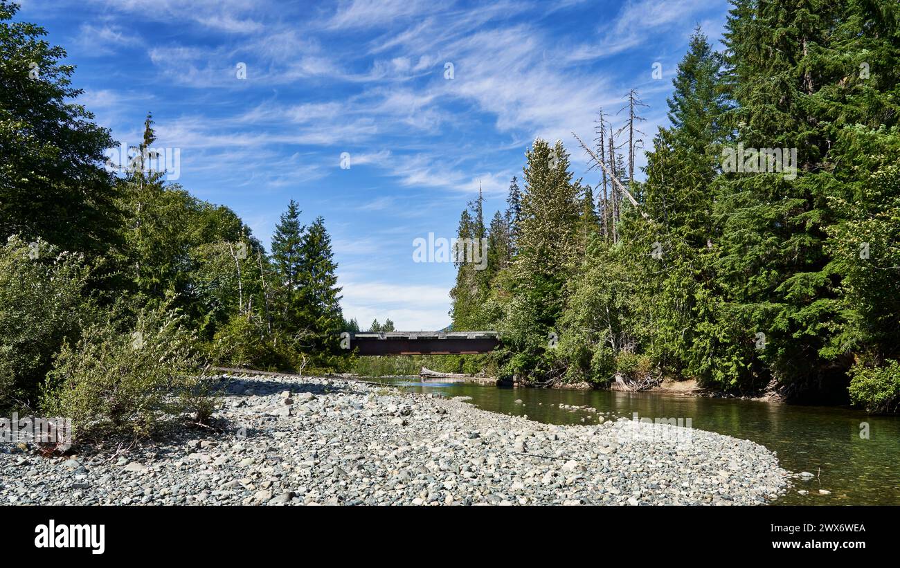 Looking down a river to a remote logging road bridge with wispy clouds ...