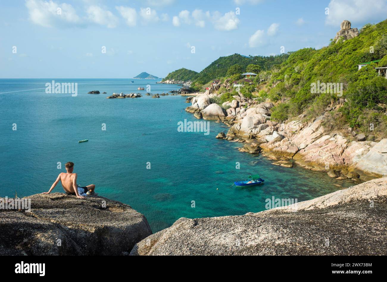 Young man tourist sitting on rock vew from back enjoying turquoise clear water tropical island ...