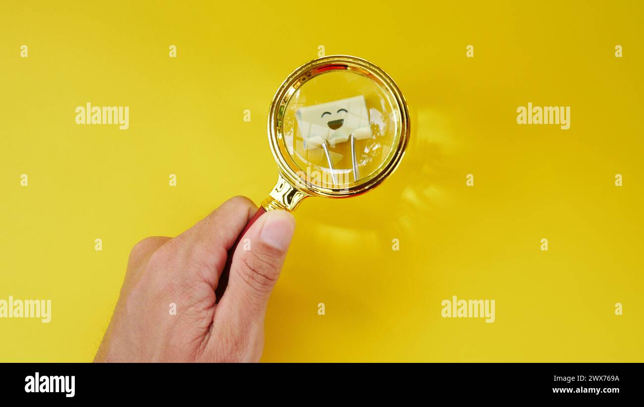 Hand-holding magnifying glass highlighting smile emoticon paper clip ...