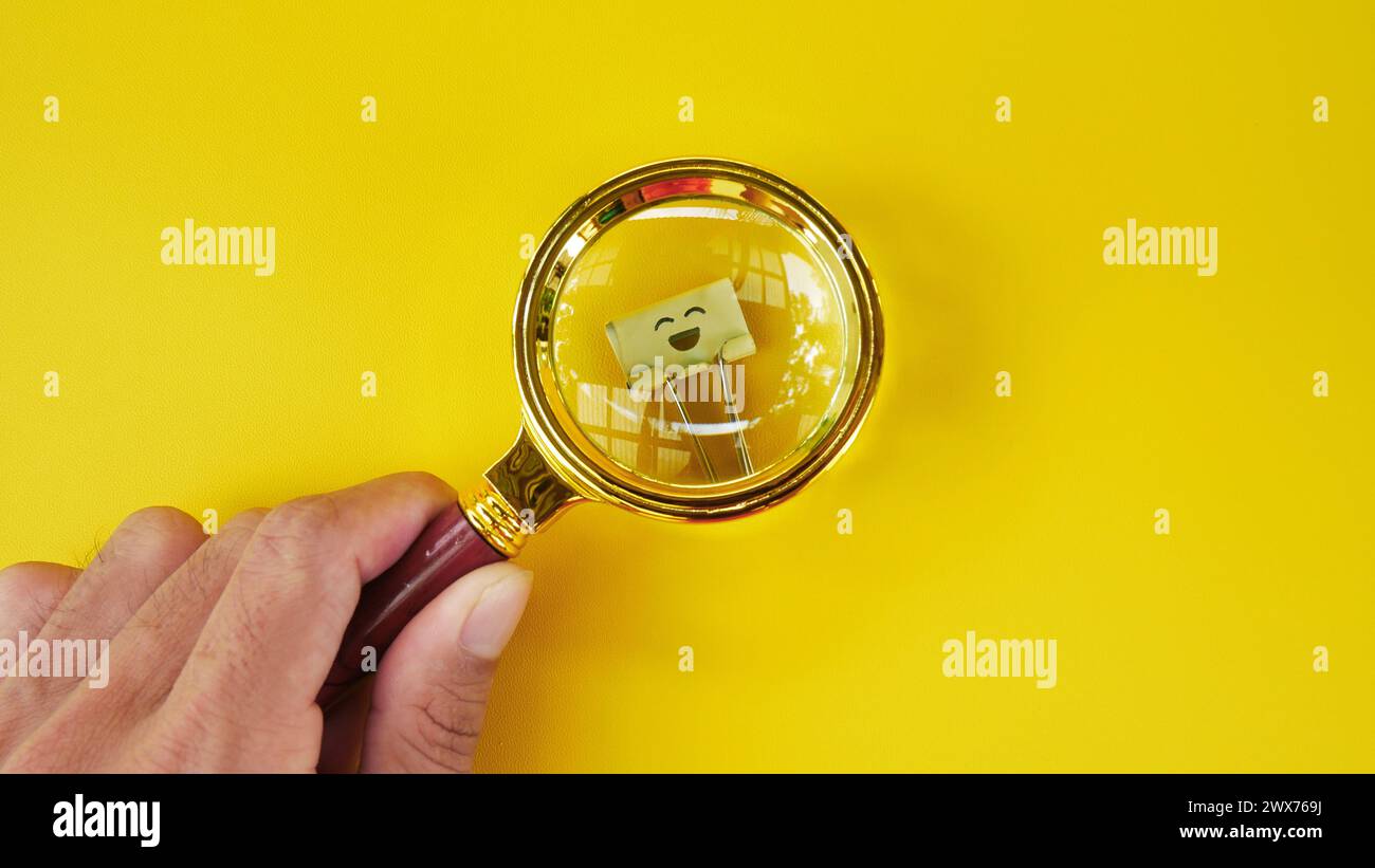 Hand-holding magnifying glass highlighting smile emoticon paper clip ...