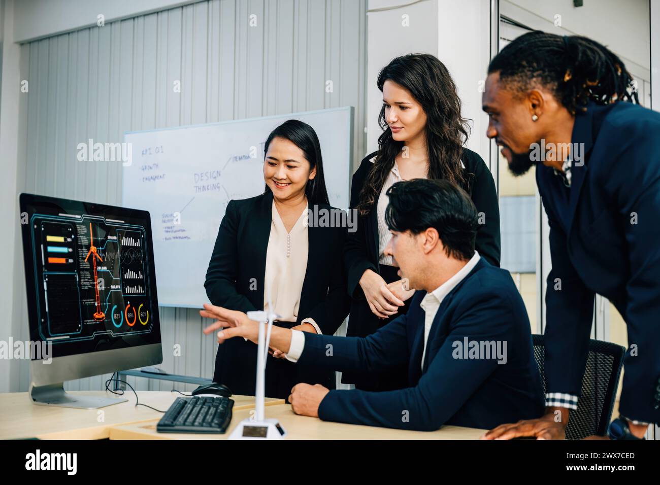 A team of professionals gathers around a desktop computer, engaging in ...