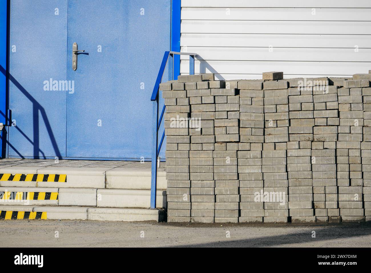 A stack of paving slabs is neatly arranged in front of a blue garage ...