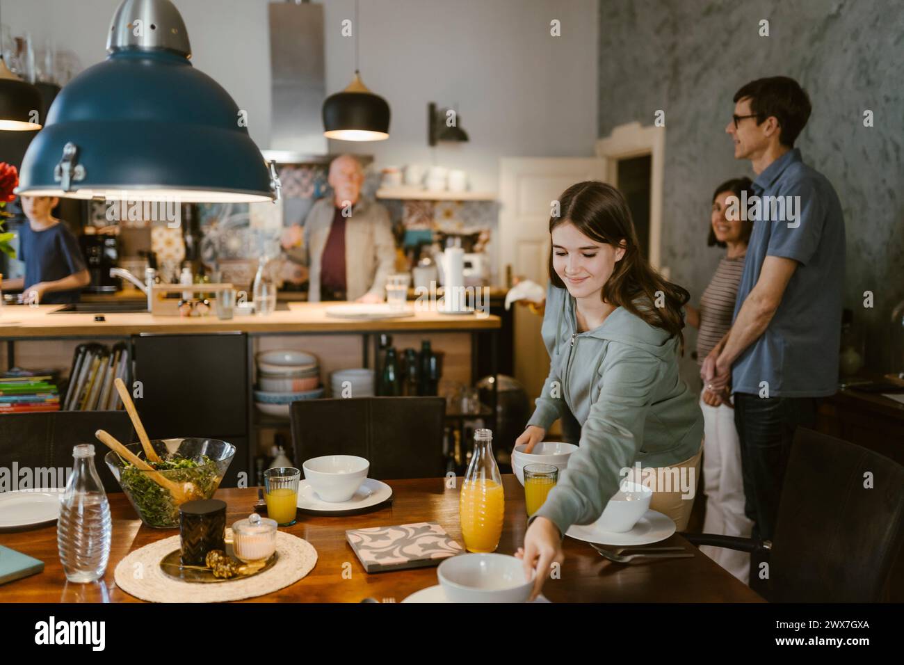 Smiling teenage girl placing bowls on dining table for dinner with ...