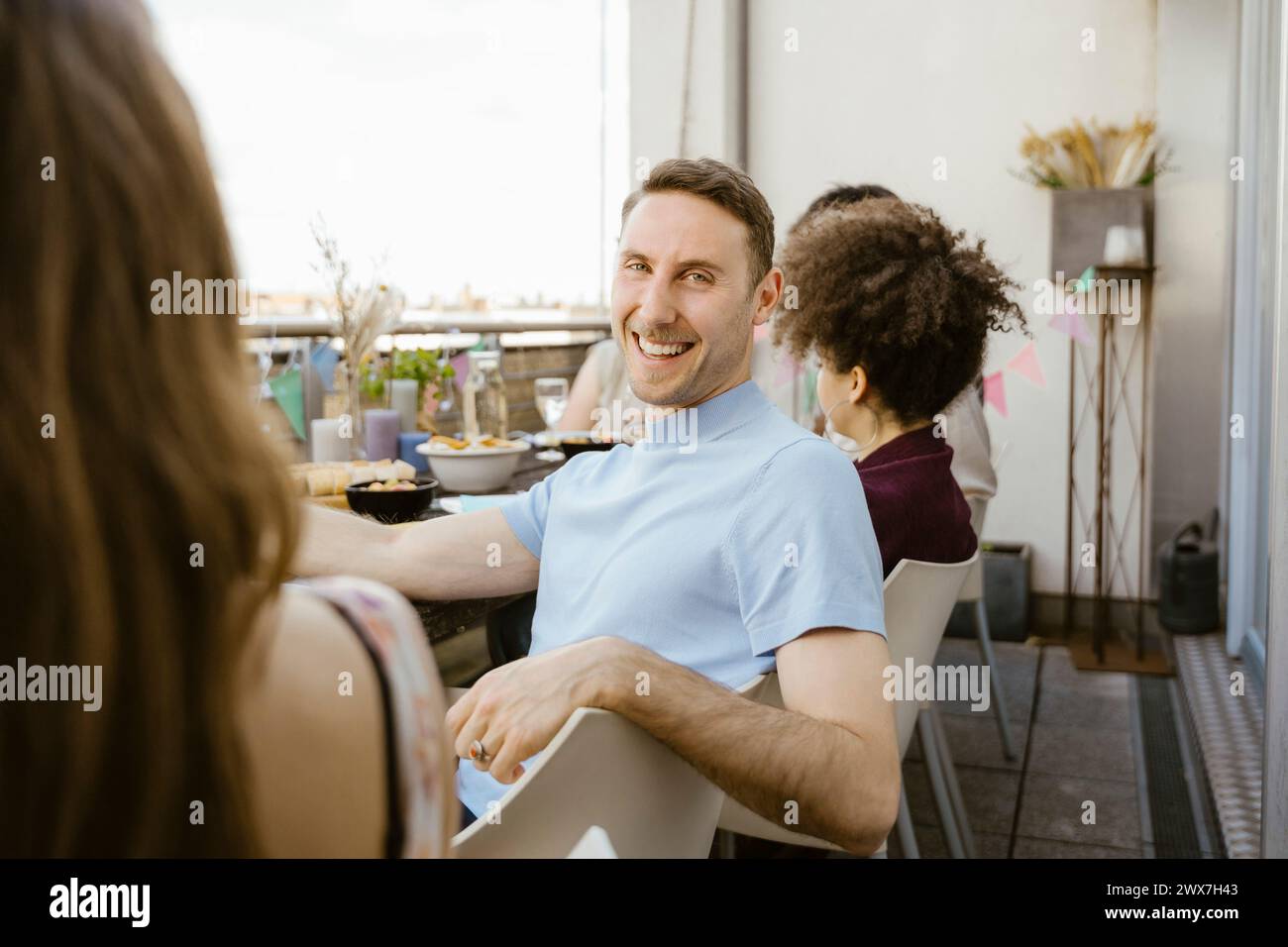 Portrait of happy man sitting on chair with male and female friends ...