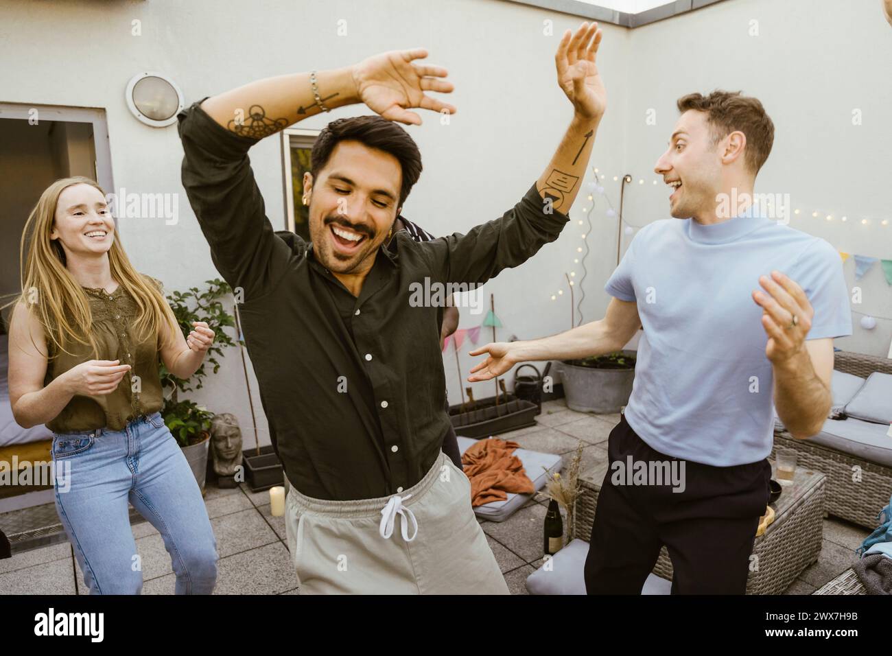 Happy man with arms raised dancing with male and female friends at ...