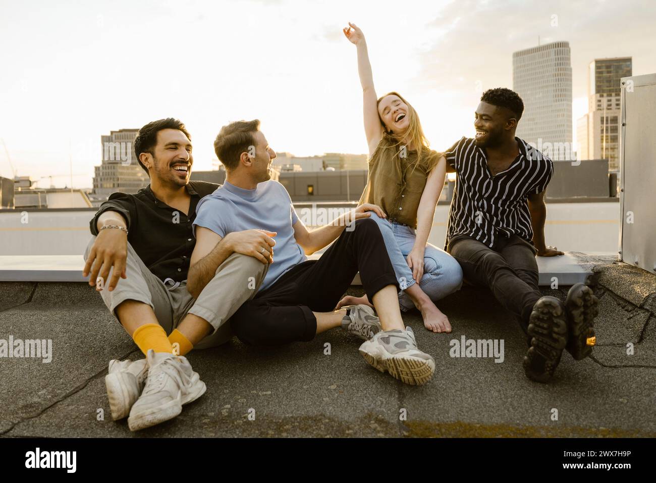 Happy woman raising hand while sitting with male friends on terrace ...