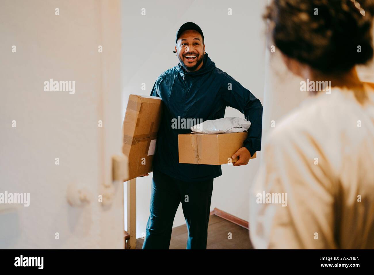 Happy male delivery person arriving with parcels at doorstep Stock ...