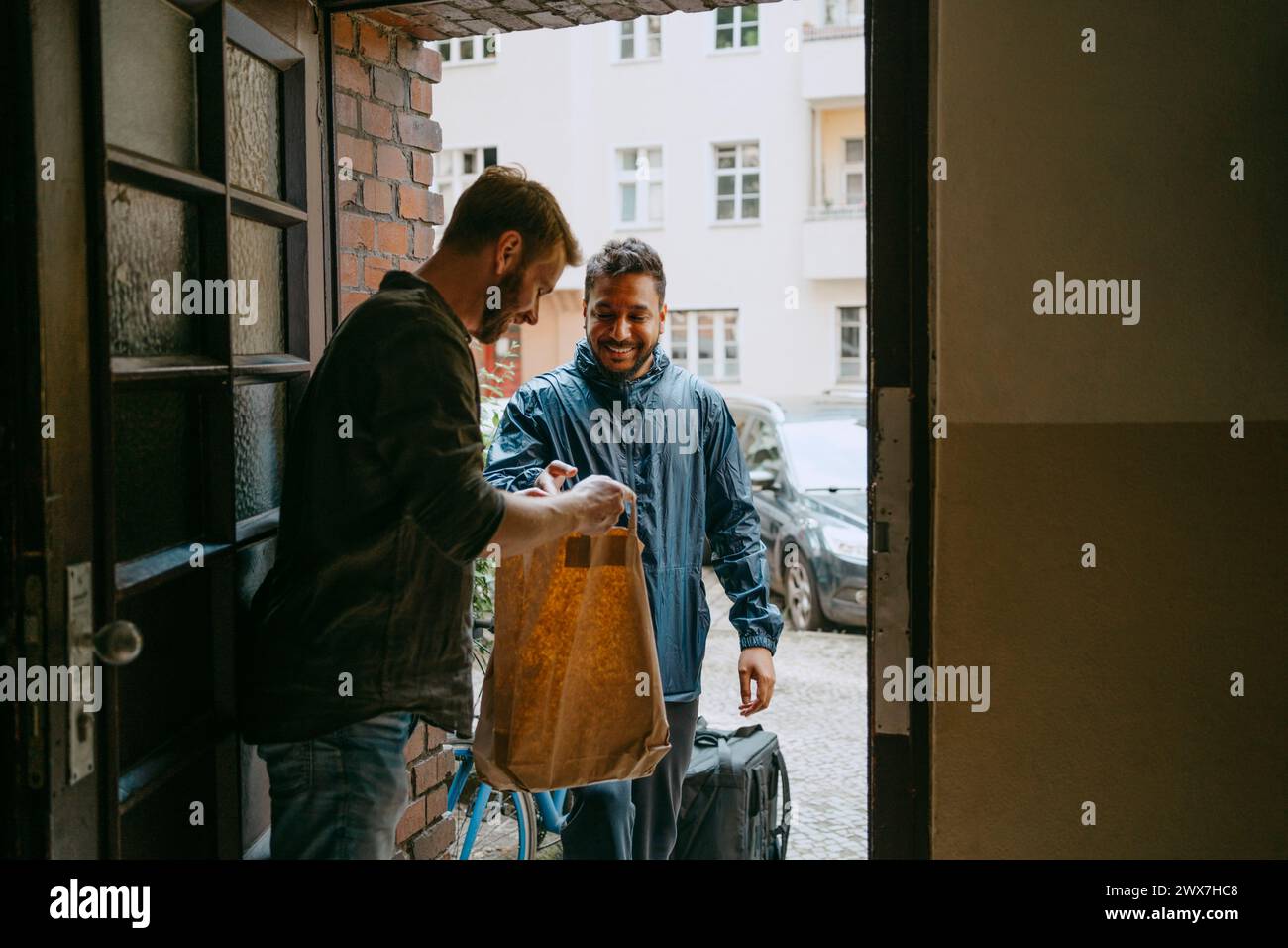 Side view of man receiving parcel from delivery person while standing ...