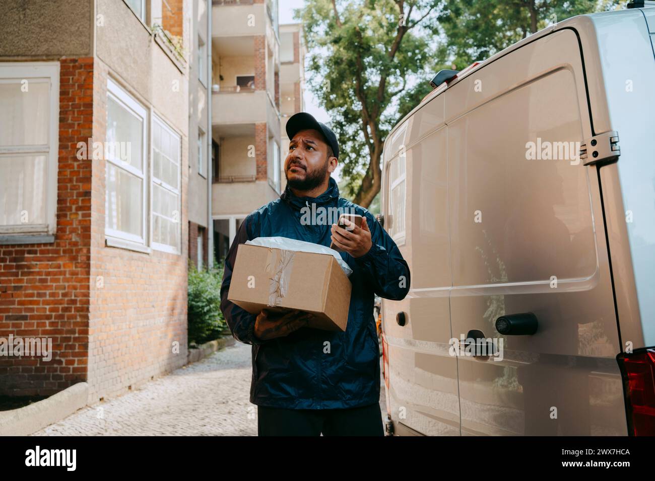 Confused male courier delivery person holding package while standing ...