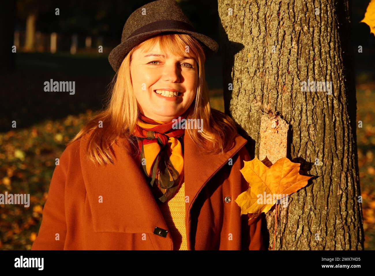 A stylish lady in a charming hat smiling amidst the picturesque autumn ...