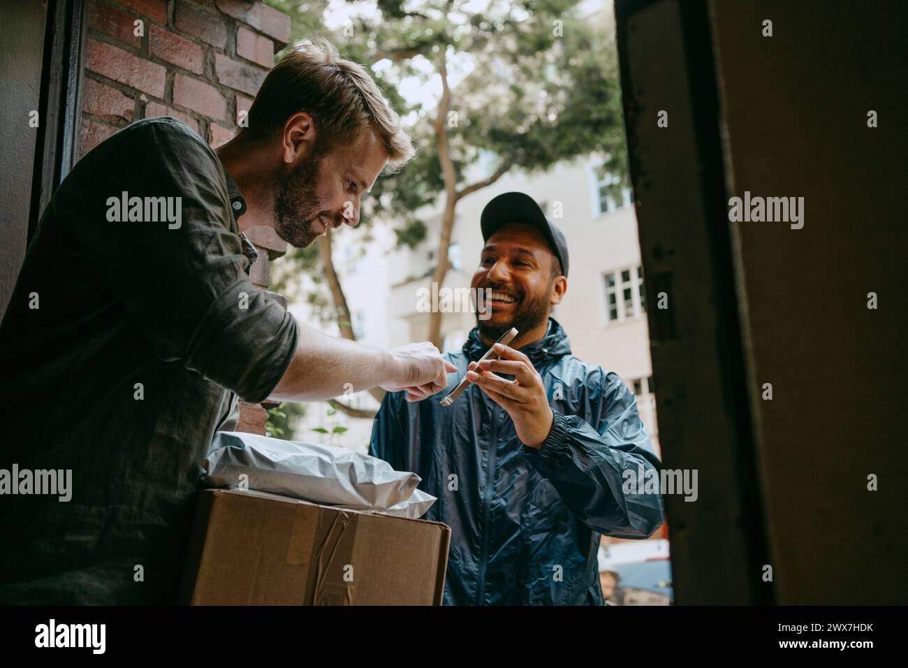Smiling delivery person taking electronic signature from man while ...