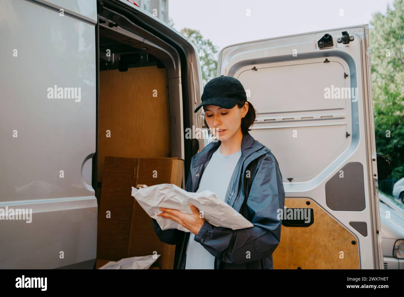 Female delivery person sorting parcel while standing near van trunk ...