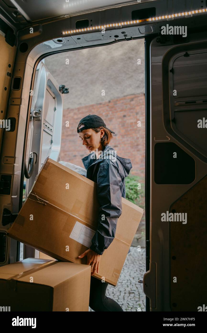 Side view of female delivery person unloading box from van trunk Stock ...