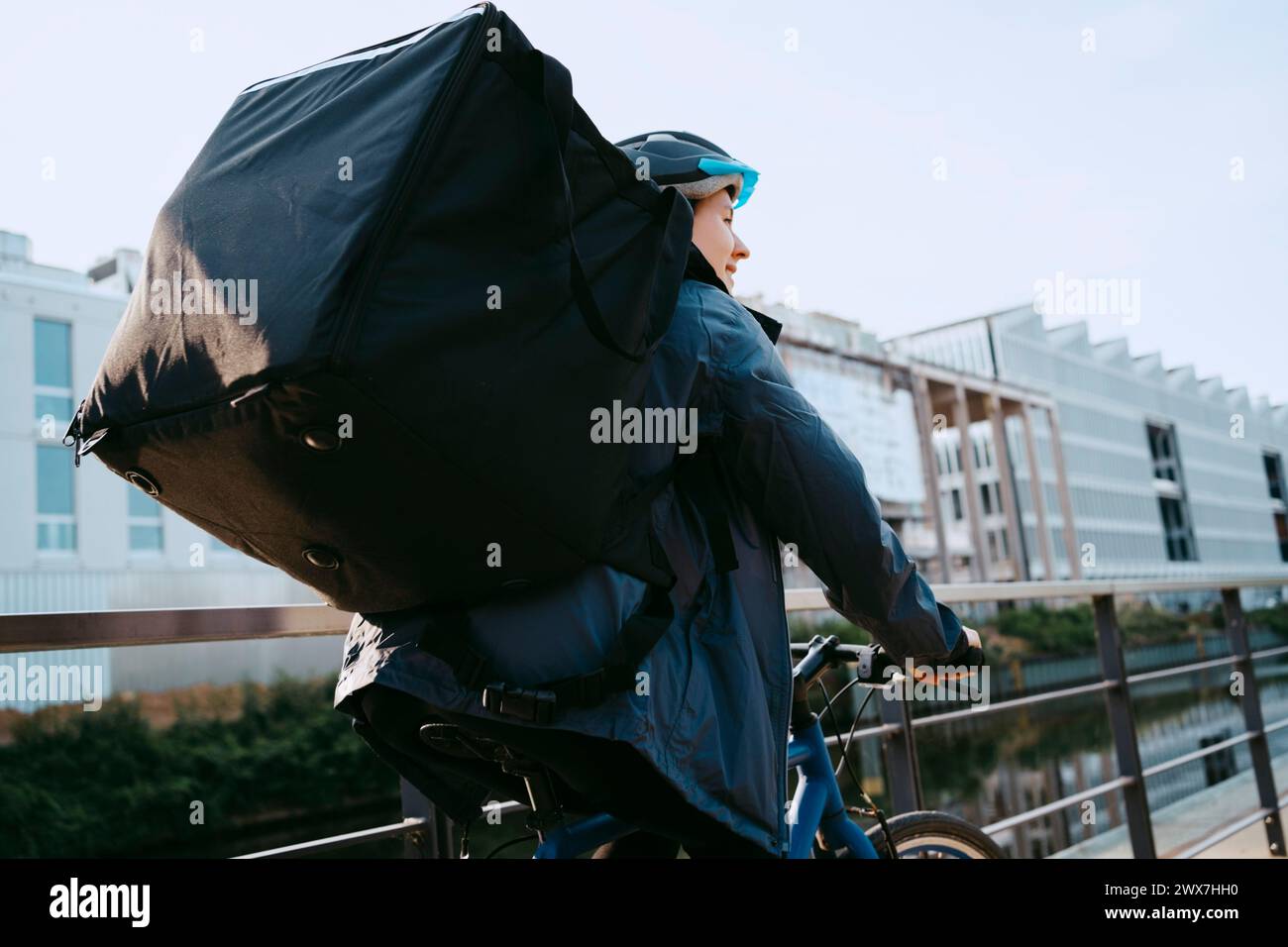 Female delivery person carrying backpack and cycling on street in city ...