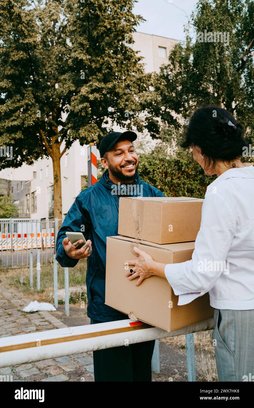 Smiling male delivery person talking with woman while delivering ...
