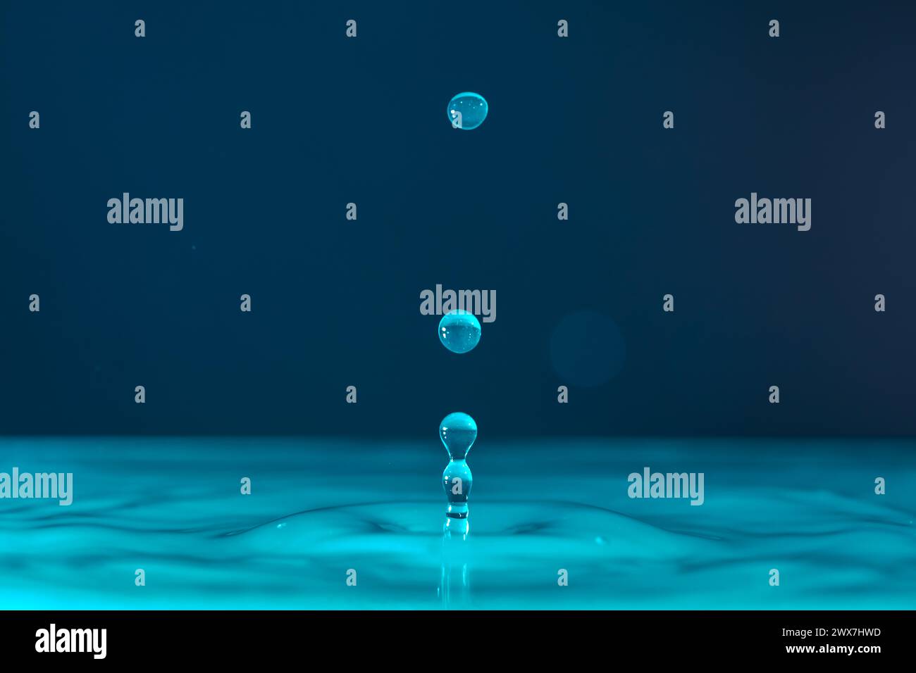 Water droplets fall down closely into the dark blue water, making it ...