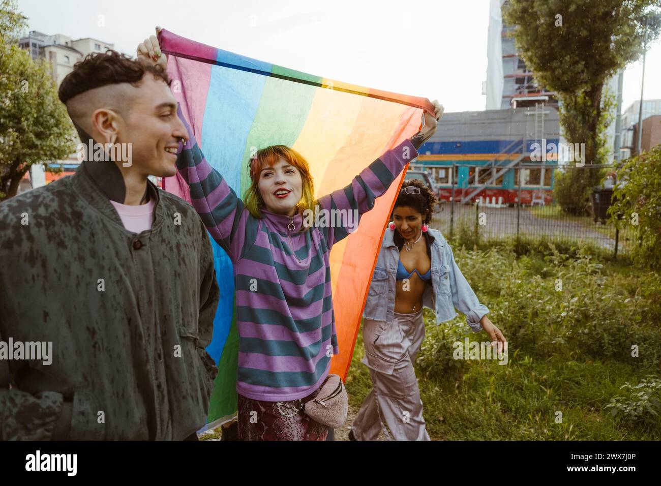 Woman holding LGBT flag while walking with non-binary friends at park ...