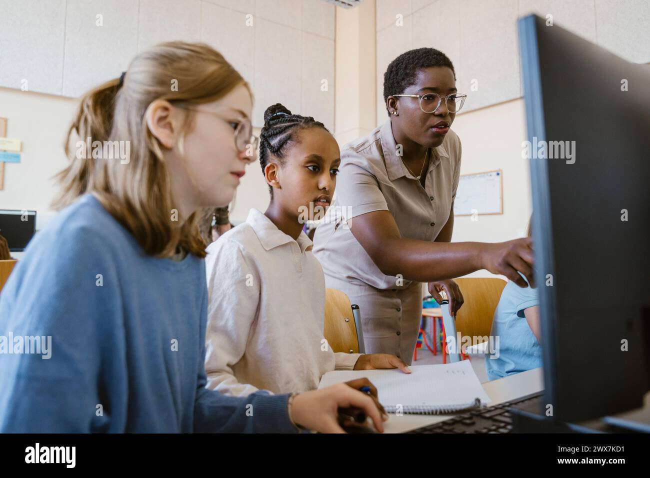 Female teacher explaining students over computer in classroom at school ...