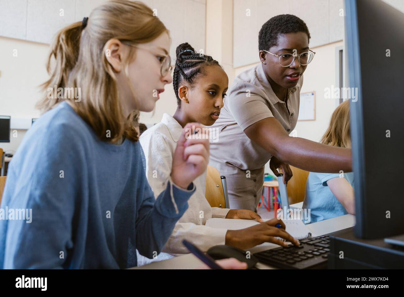 Female teacher pointing at computer while teaching students in ...