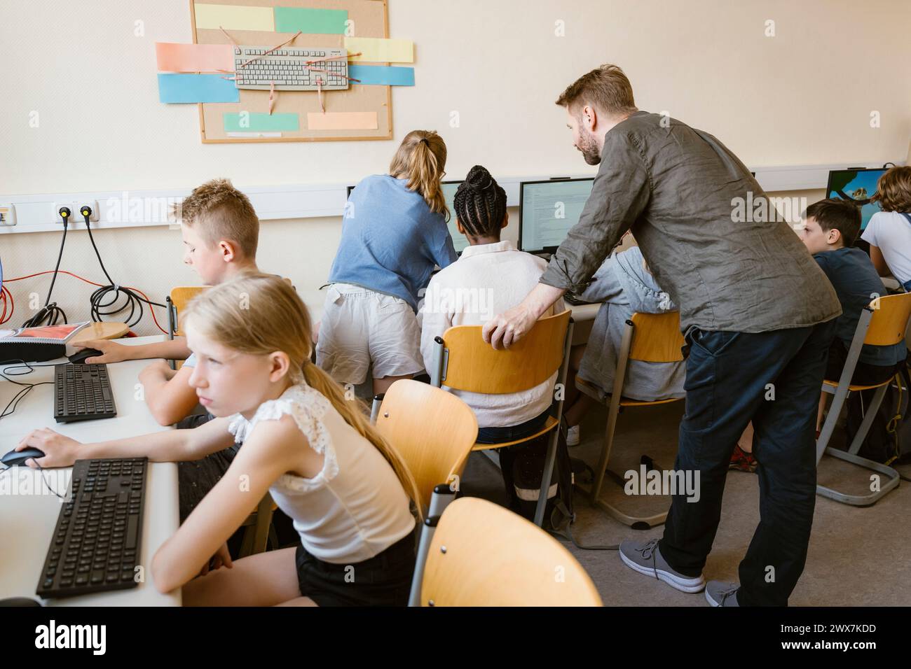 Male teacher with students learning through computers in classroom at ...