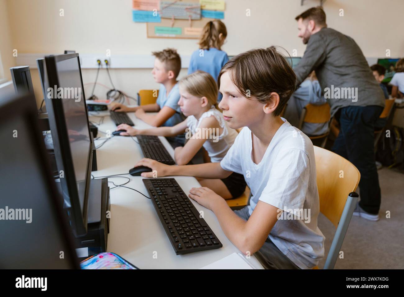 Concentrated male pupil using computer while sitting with students at ...