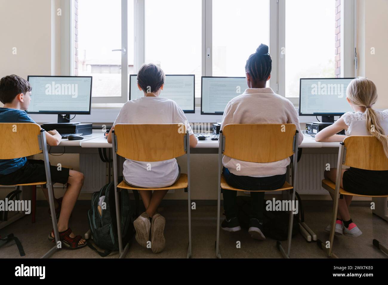 Rear view of male and female students using computers while sitting in ...