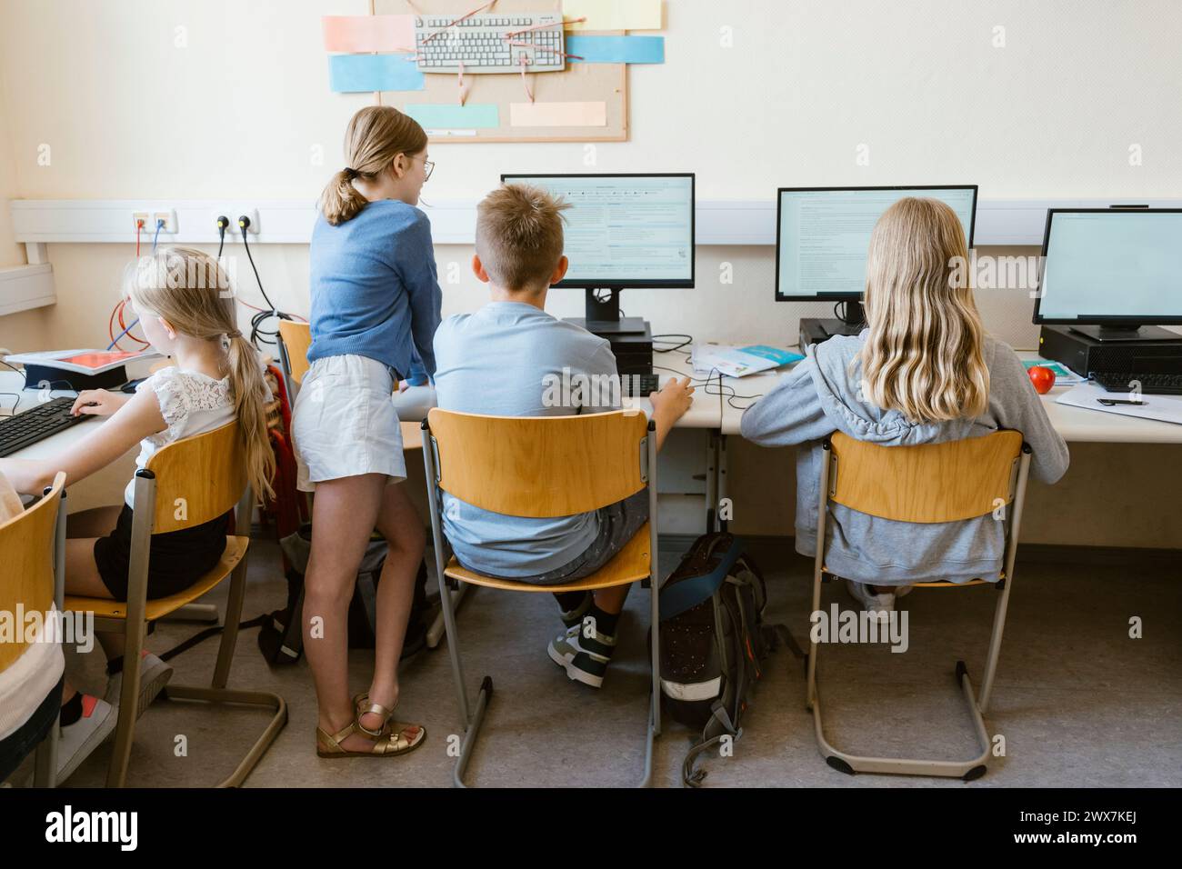 Male and female pupils using computers while sitting on chairs in ...