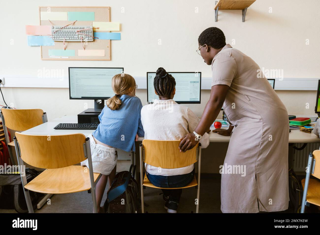 Side view of female teacher explaining girls using computer while ...