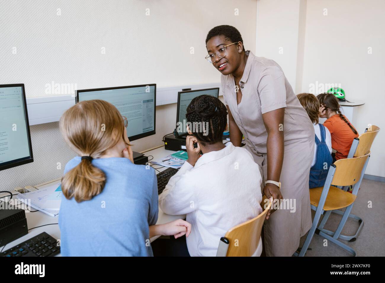 Female teacher talking with children sitting in computer class at ...