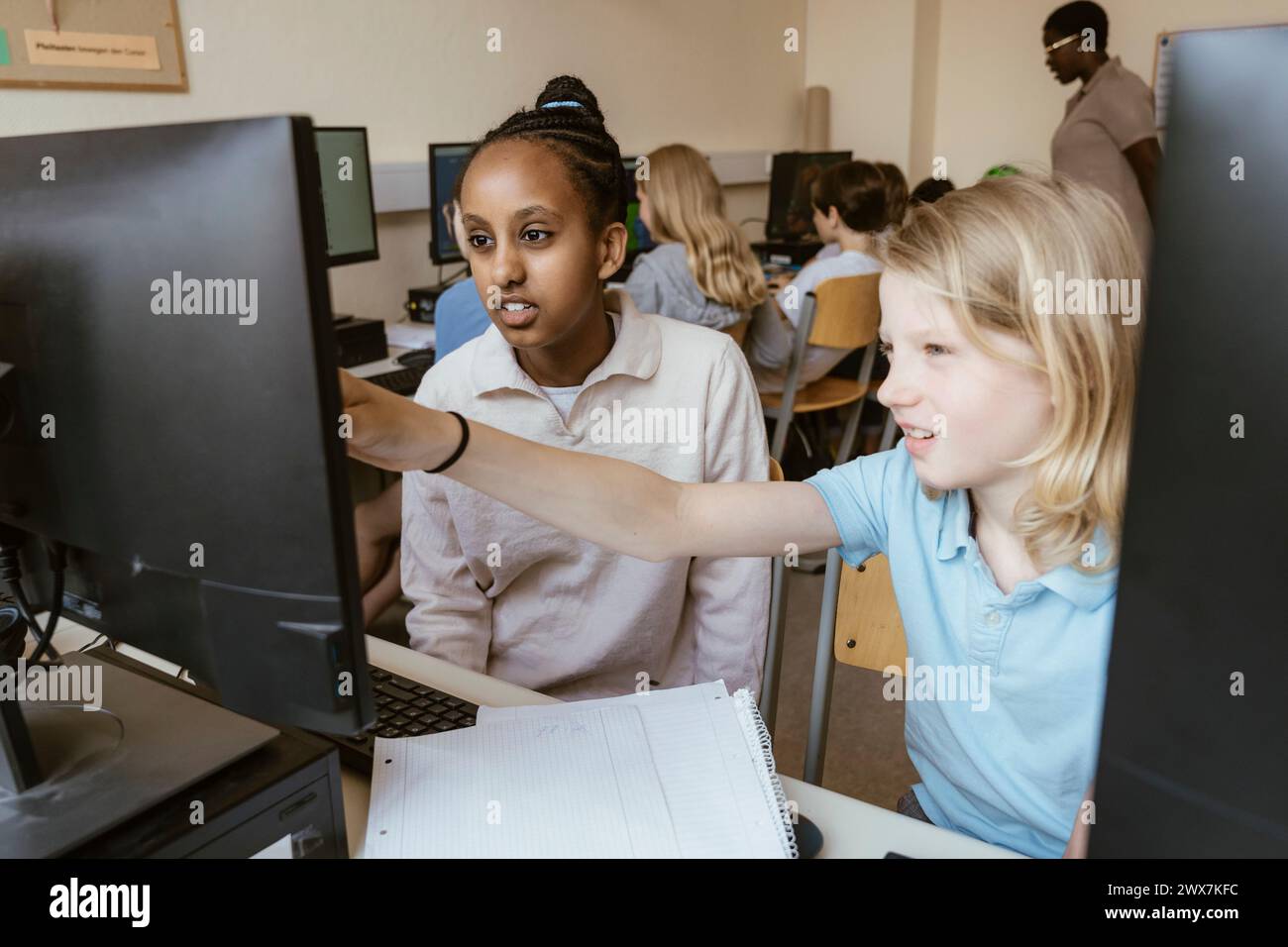Girl pointing at computer monitor while sitting with female friend in ...