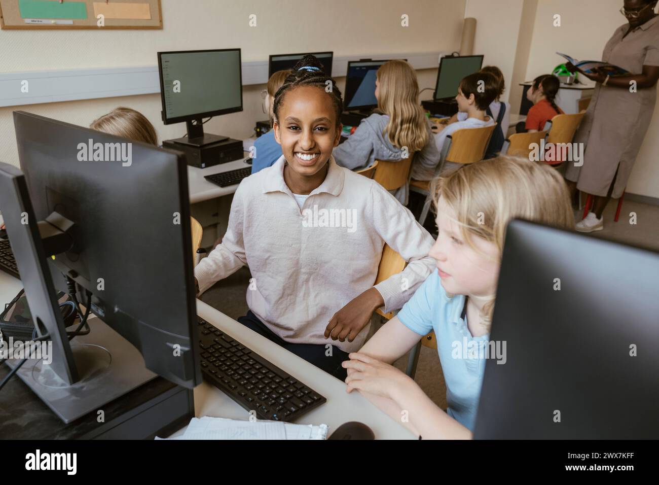 Portrait of smiling girl sitting on chair with friends in computer ...
