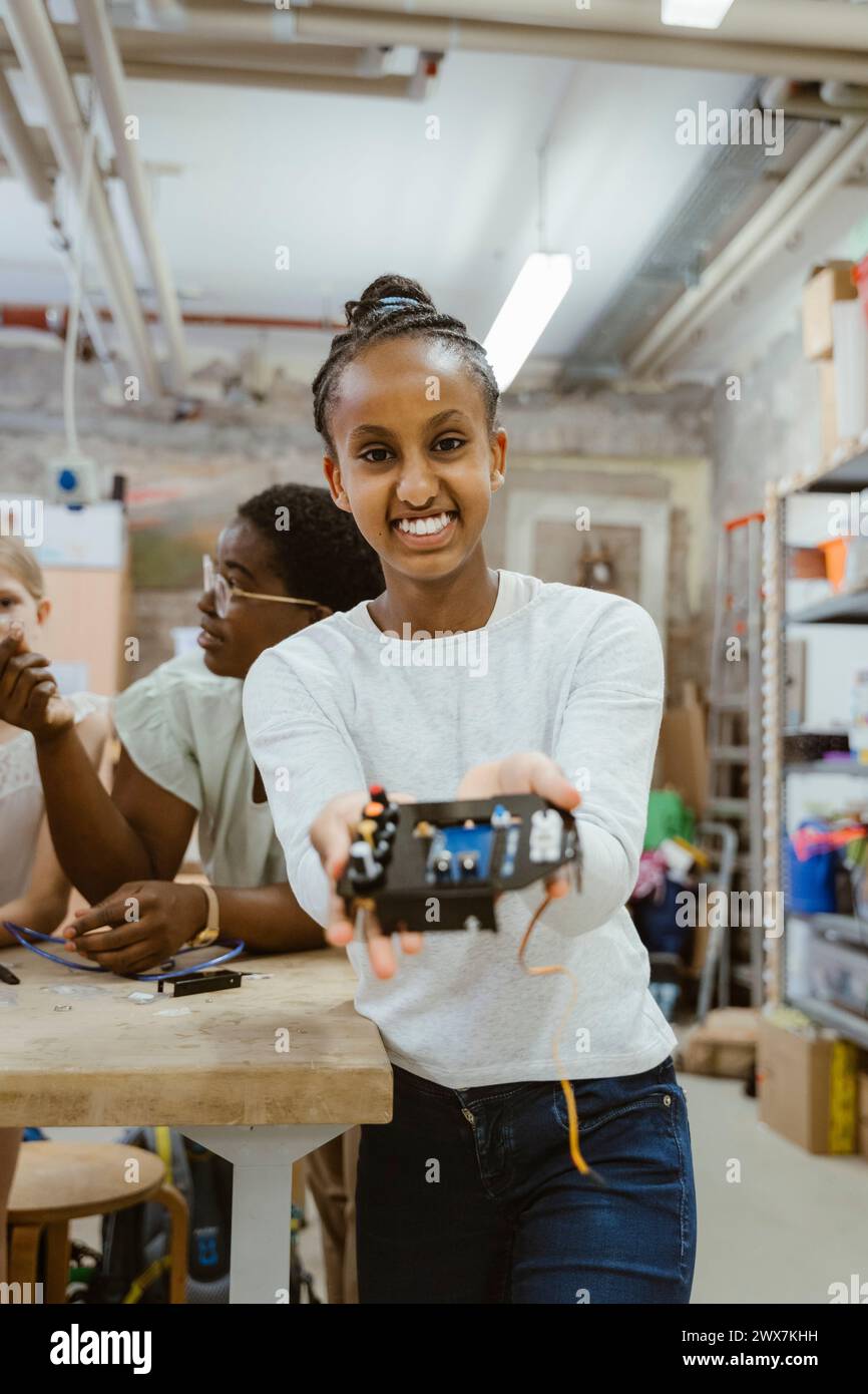 Portrait of smiling girl showing electric component in technology ...