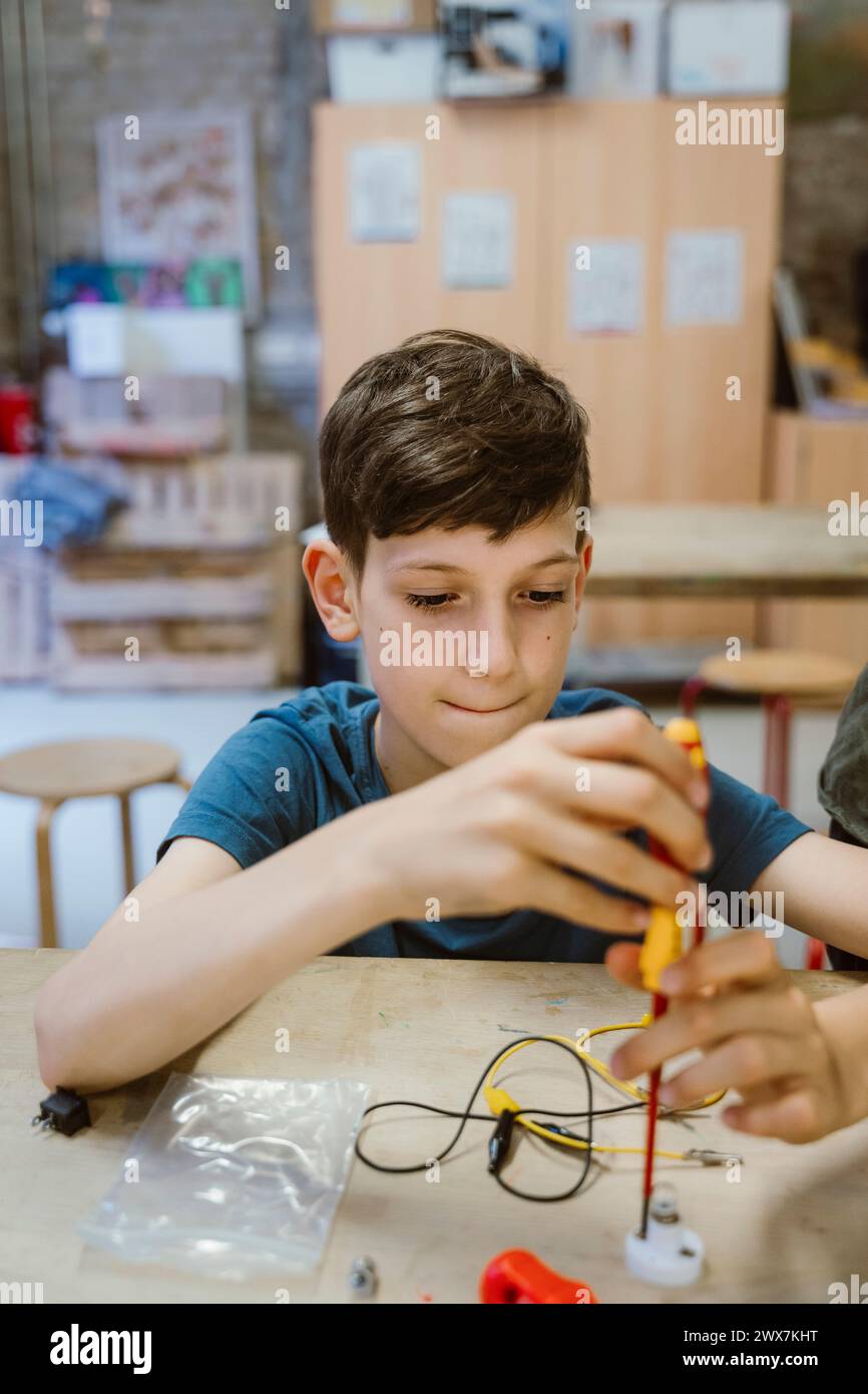 Boy tightening screw on electrical part using screwdriver on table at ...
