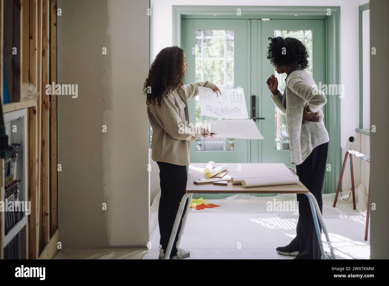 Side view of client and female architect comparing blueprints while ...