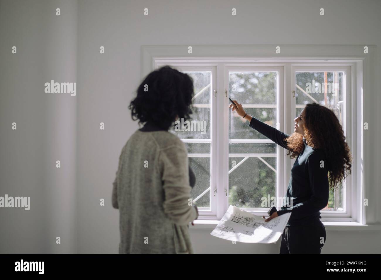 Female architect pointing at window while talking to client at under ...