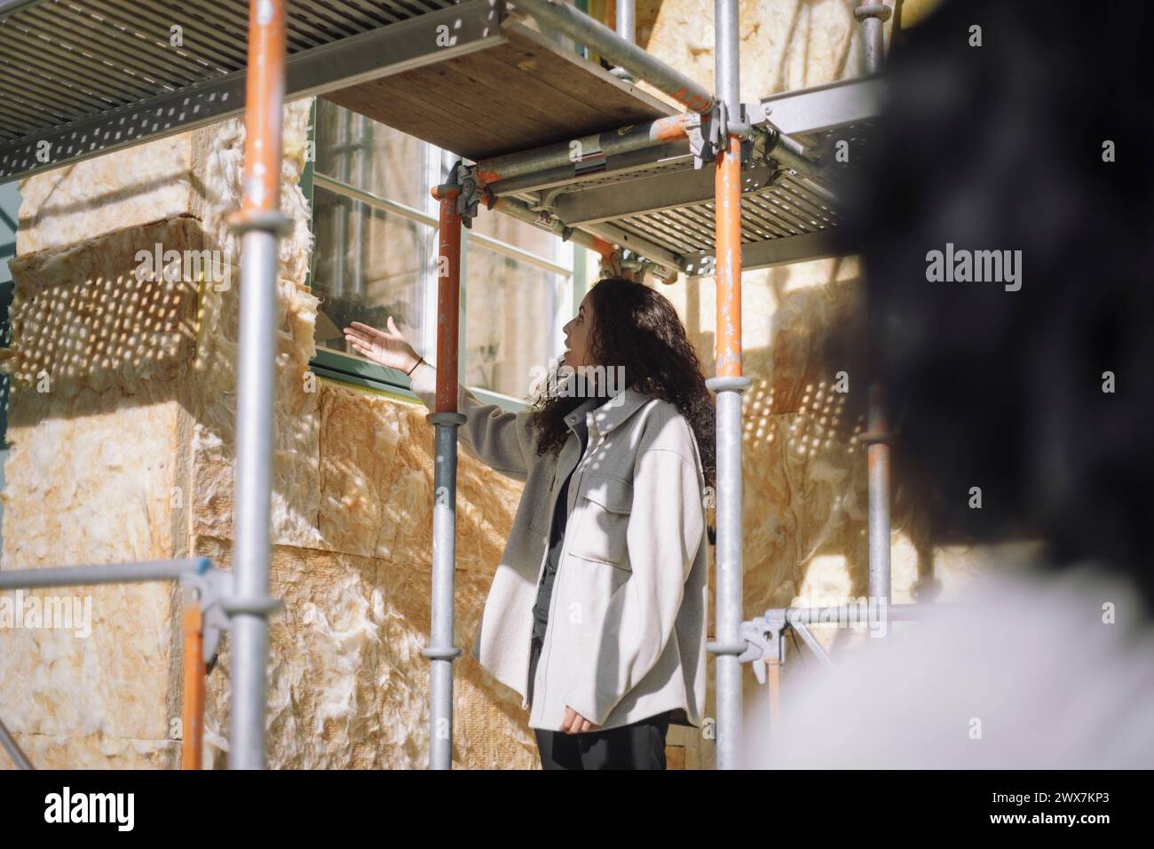 Female architect talking to client while standing under scaffolding at ...