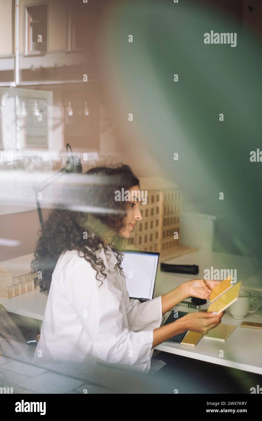 Side view of female architect comparing color samples while sitting at ...