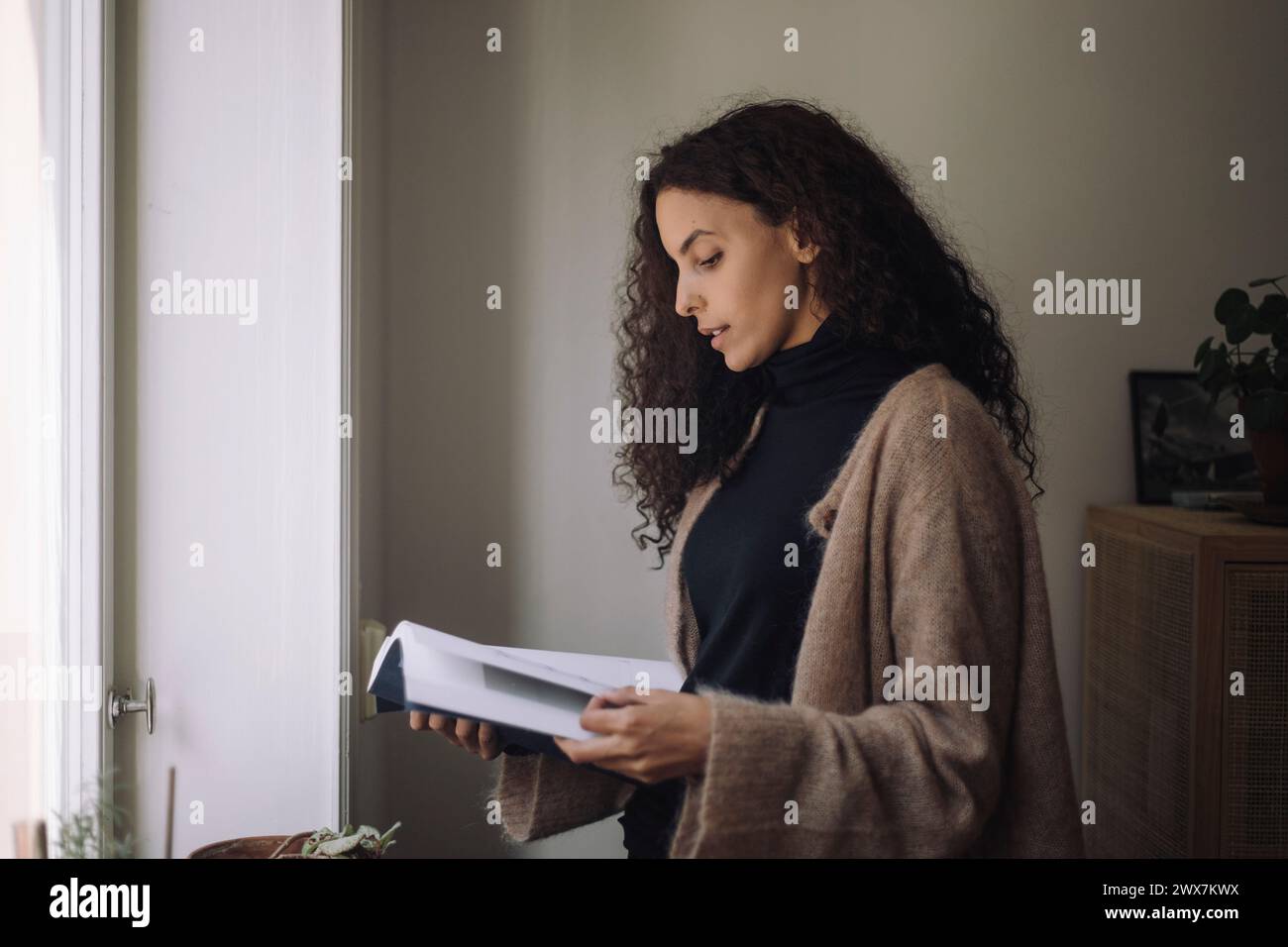 Female architect with curly hair reading book at home Stock Photo - Alamy