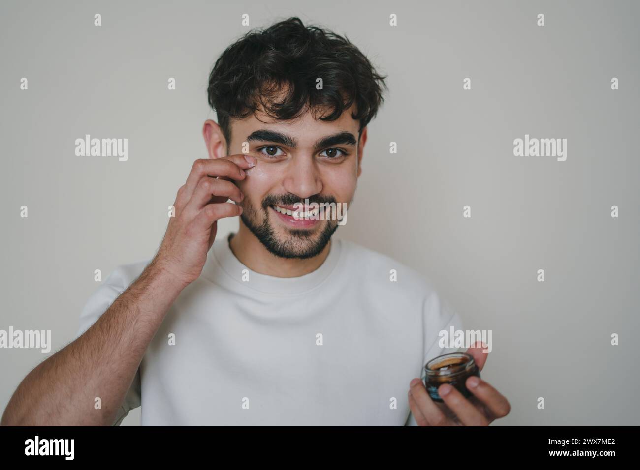 Good looking young man putting on some anti-aging cream to prevent bags ...