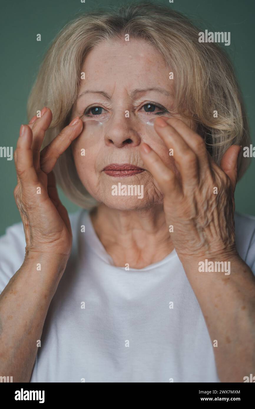 Positive senior woman applying collagen eye patches on her face while ...
