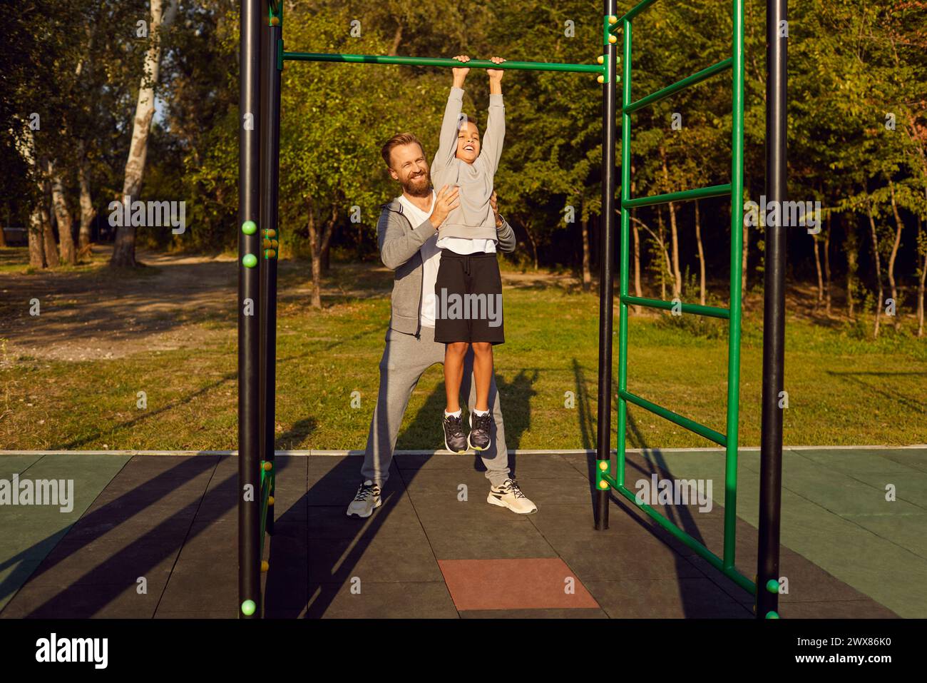 Happy father and little son doing pull ups on sports ground in green ...