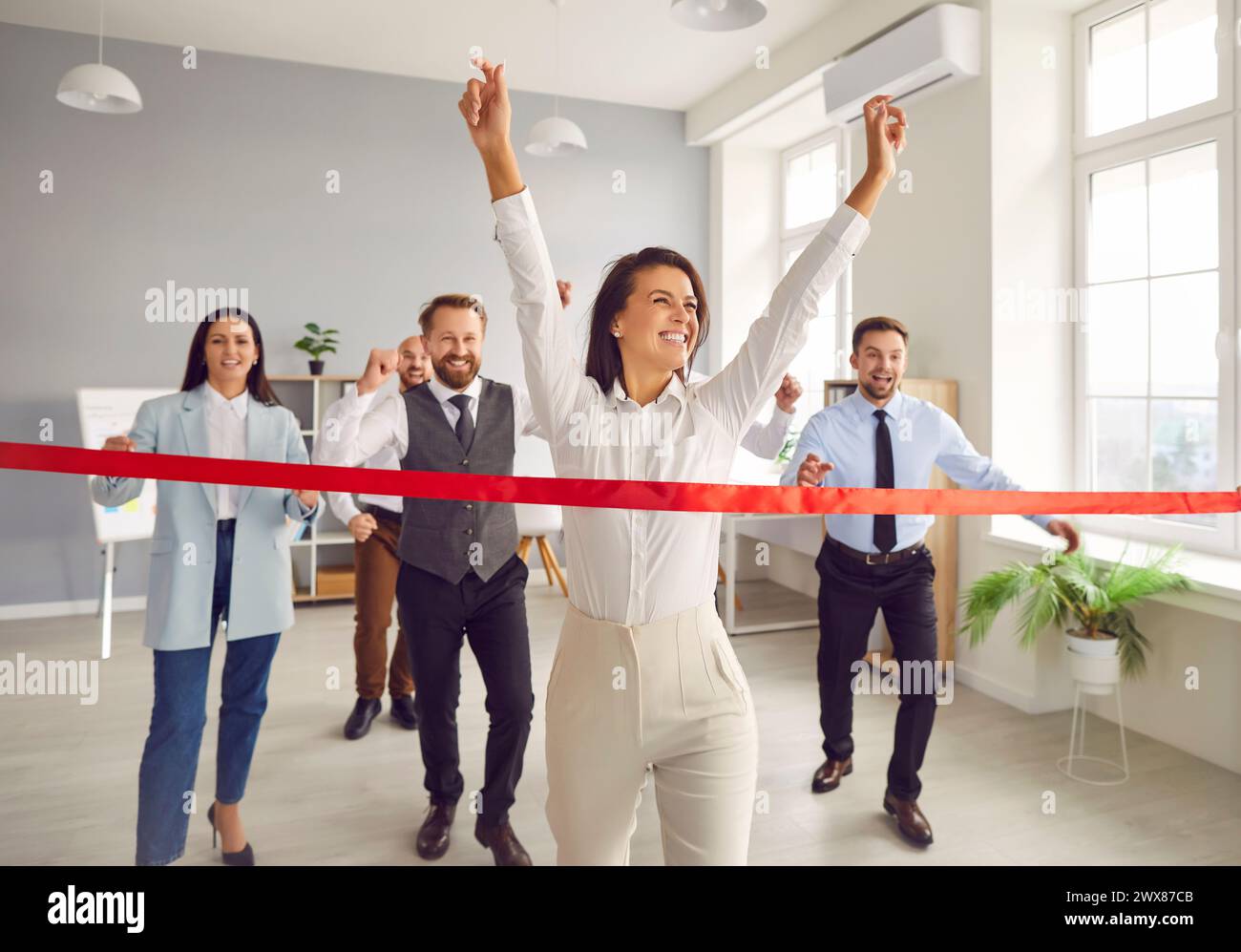 Woman running to red ribbon in office with people colleagues in ...