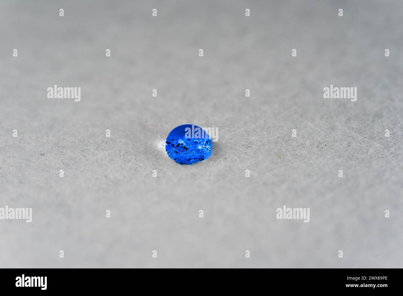 blue drop of water looking like a glowing stone on top of a sheet of ...