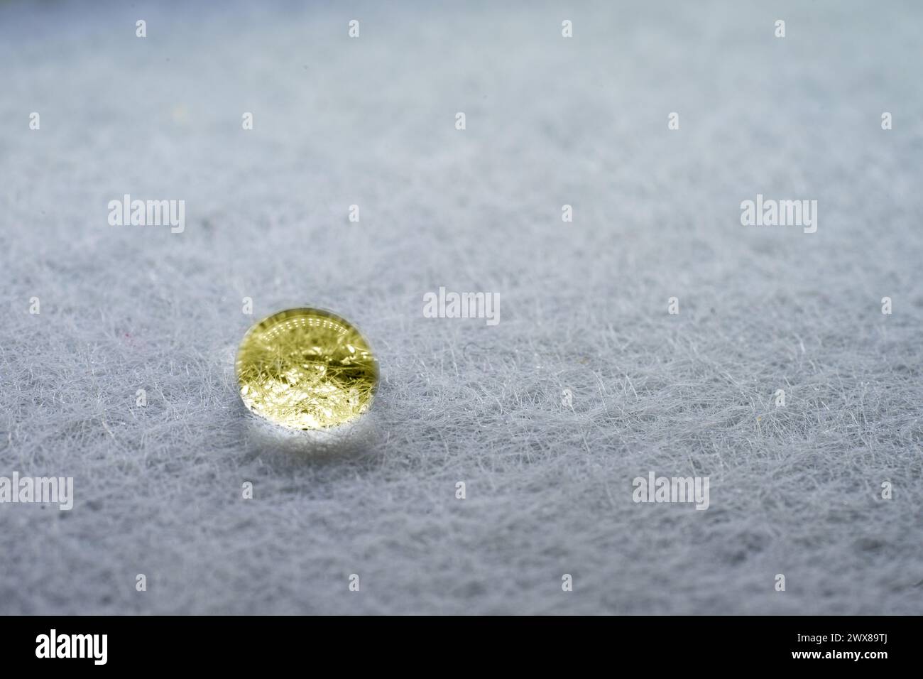 Yellow water drop looking like a glowing stone on top of white fabric ...