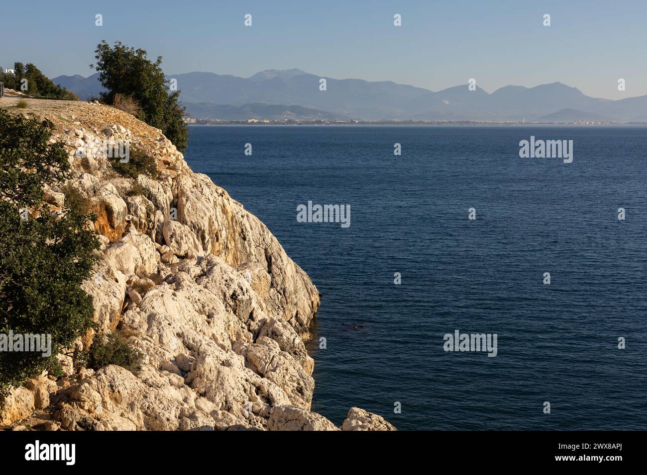 Limestone cliff adorned with greenery towers above the serene blue ...
