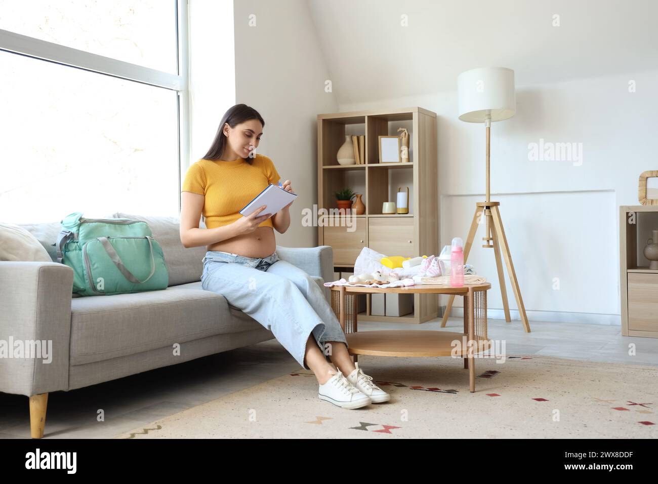 Young pregnant woman with maternity hospital bag writing checklist on ...
