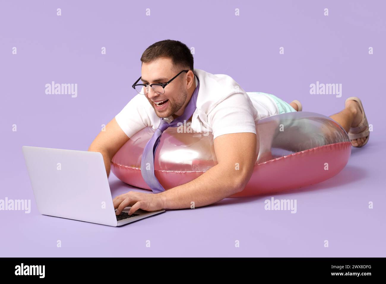 Happy office worker with laptop lying on inflatable ring against lilac ...