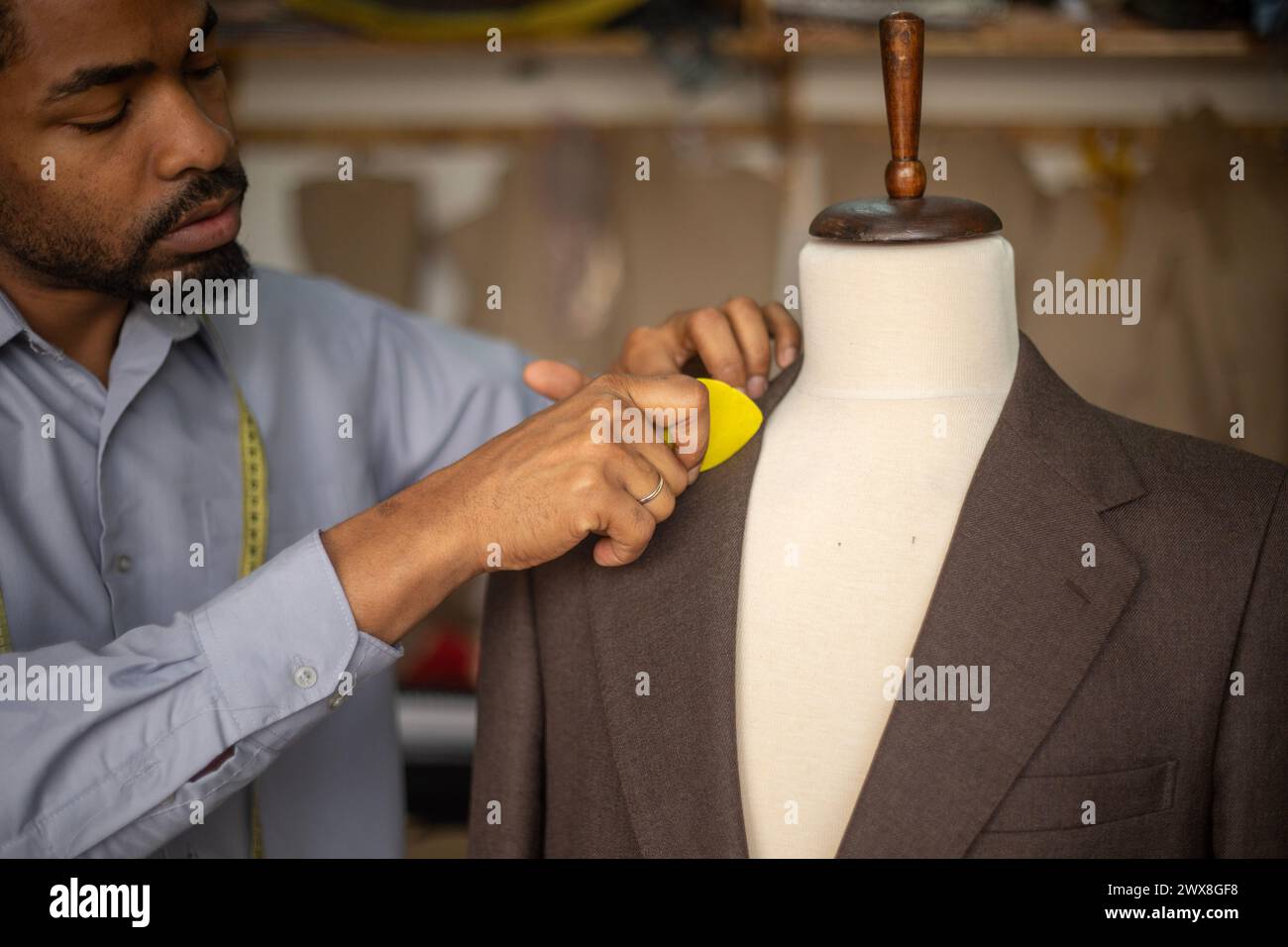 Young African American tailor at work measuring and marking jacket collar, Bespoke tailor at ...